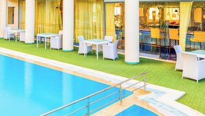 Uma área junto à piscina com mesa e cadeiras de vidro, uma piscina e um bar com cortinas amarelas.