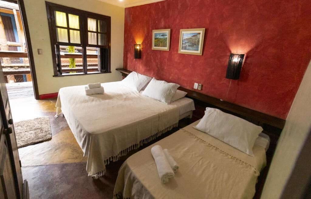 Quarto de hotel com duas camas, uma parede vermelha e uma janela com cortinas.