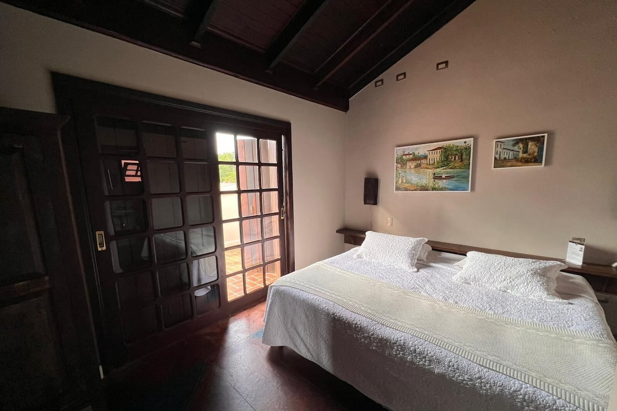 Quarto com uma cama grande, uma porta de madeira e duas pinturas na parede.