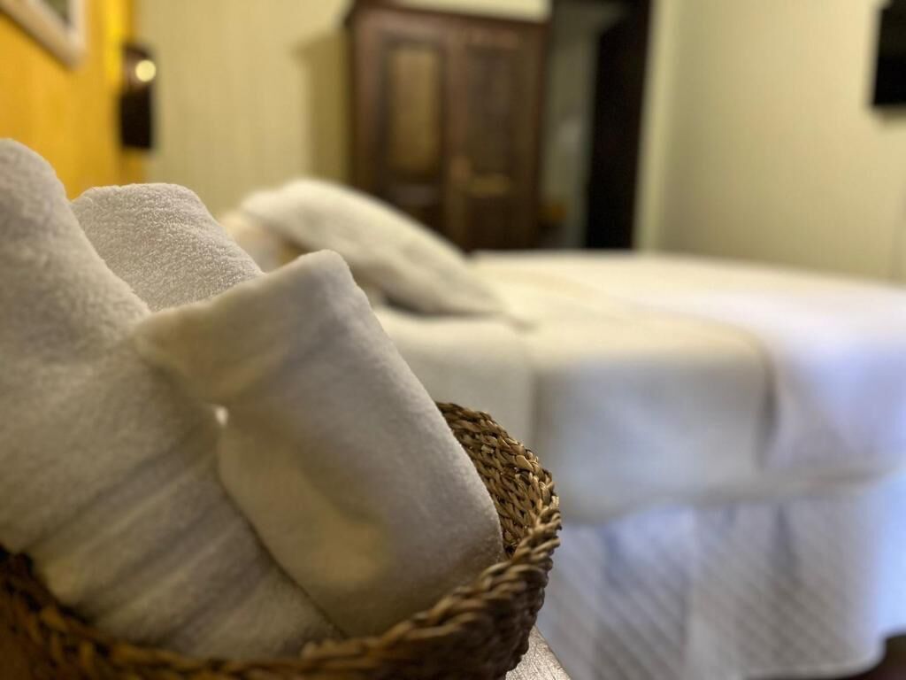 Uma cama com lençóis brancos e uma cesta de palha com toalhas dobradas.