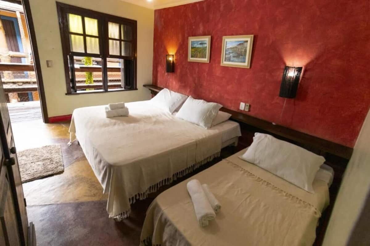Quarto de hotel com duas camas, uma parede vermelha e uma janela com cortinas.