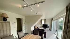 Uma sala de estar moderna com área de jantar, televisão e porta de vidro deslizante para o exterior.