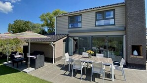 Uma casa moderna de dois andares com um alpendre que inclui uma mesa, cadeiras, churrasqueira e um espaço coberto para sentar.