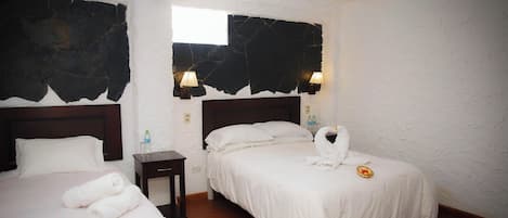 Quarto de hotel com duas camas, uma pequena mesa de cabeceira, uma luminária na parede e uma toalha em cada cama.