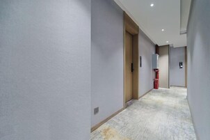 Um corredor com piso coberto por carpete, uma porta de madeira e um interruptor de luz na parede.