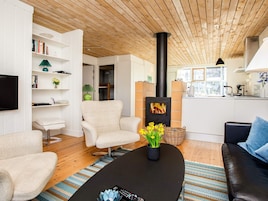 Uma sala de estar moderna com lareira, assentos confortáveis e área de cozinha visível por uma porta aberta.