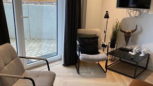 Uma sala de estar moderna com um sofá, uma poltrona, uma mesa de centro e uma TV fixada na parede.