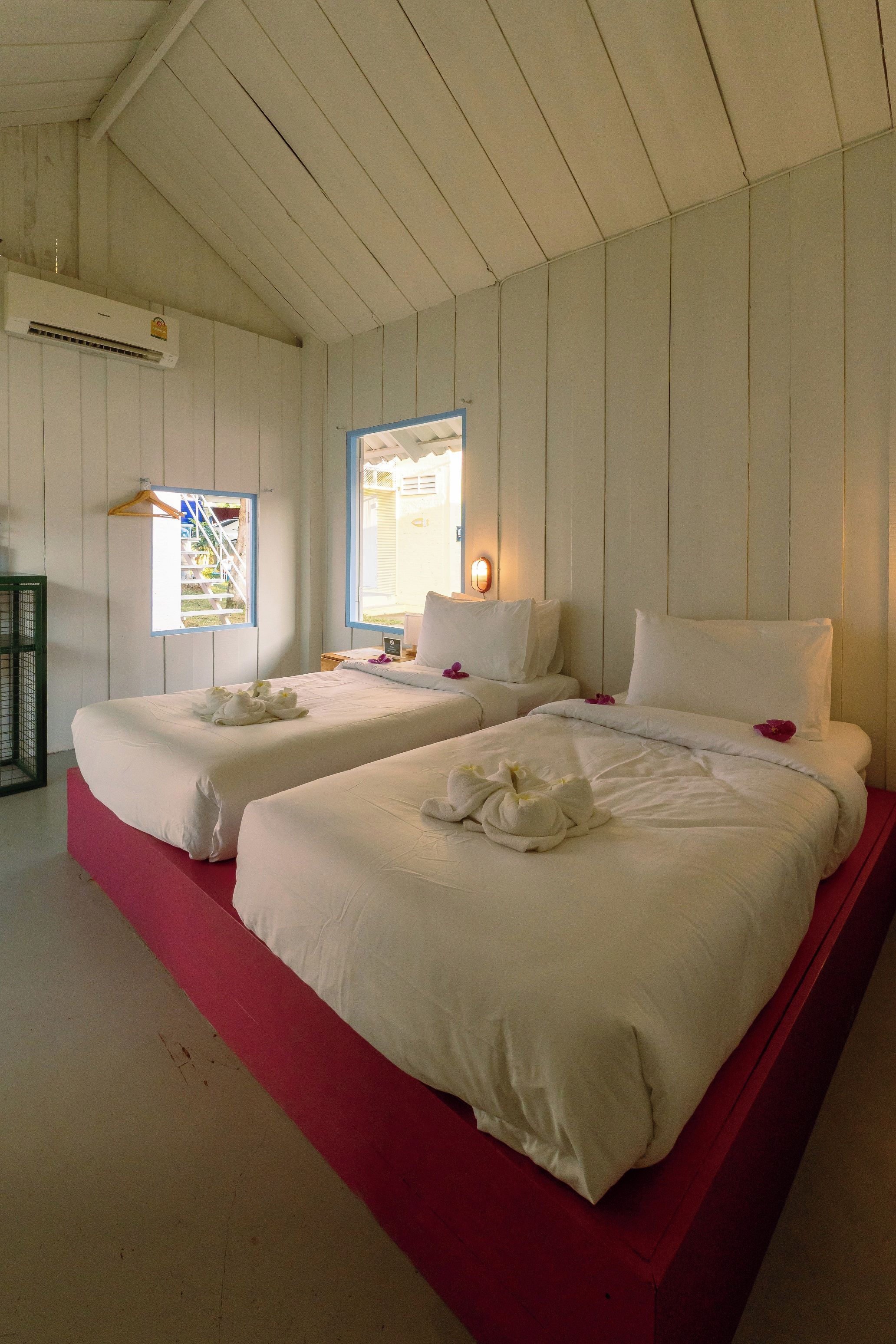 Quarto com duas camas, cada uma com roupa de cama e toalhas brancas, teto de madeira e janela com vista.