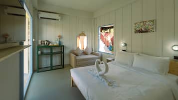 Quarto de hotel com cama, escrivaninha, cadeira, janela e ar-condicionado fixado na parede.