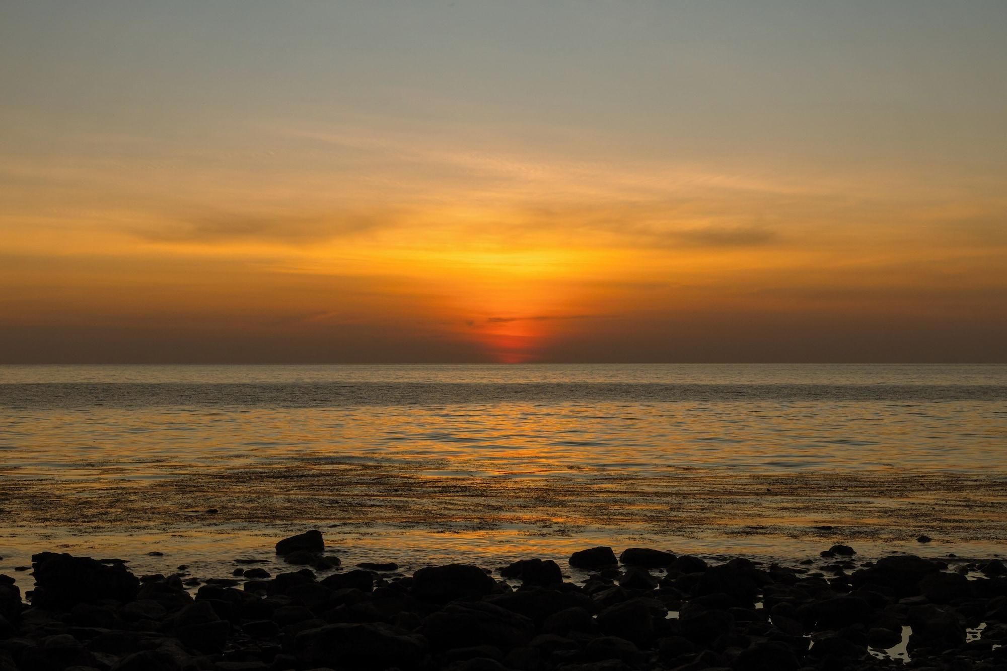 Um pôr do sol sobre um mar calmo com uma costa rochosa.