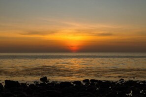 Um pôr do sol sobre um mar calmo com uma costa rochosa.