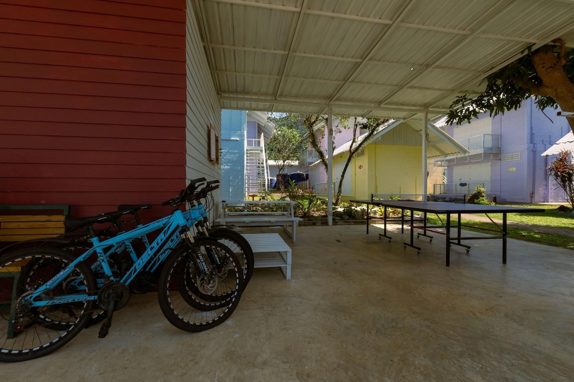 Área externa coberta com mesa e cadeiras, uma bicicleta azul e um edifício ao fundo.