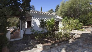 Um edifício rústico de pedra com fachada branca, rodeado por árvores e um caminho de pedra.