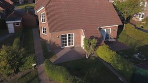 Uma casa de dois andares com telhado de telhas vermelhas, varanda frontal e um pequeno jardim.