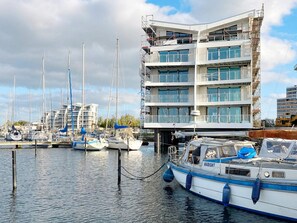Marina com vários barcos atracados, um edifício em construção com andaimes, e um céu claro.