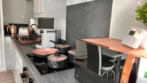 Uma cozinha moderna com bancada preta, eletrodomésticos de aço inoxidável e uma pequena mesa de jantar.