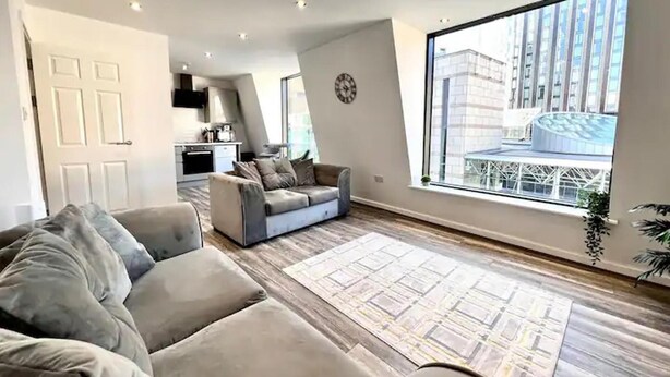 Uma sala de estar moderna com um sofá cinzento, uma mesa de centro e uma grande janela com vista para a cidade.