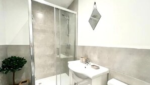 Uma casa de banho moderna com cabine de duche em vidro, lavatório branco e sanita.
