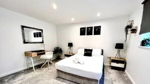 Quarto moderno com uma cama grande, uma escrivaninha e uma cadeira. Há três quadros pendurados na parede e um espelho.