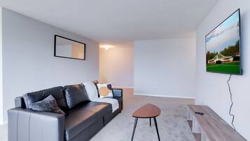 Uma sala de estar moderna com um sofá cinza, uma pequena mesa de centro de madeira e uma TV de tela plana fixada na parede.