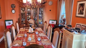 Uma sala de jantar com uma mesa comprida posta para refeição, rodeada por cadeiras.