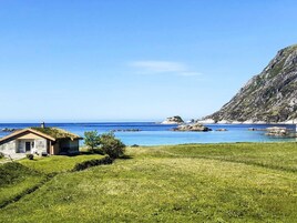 Uma propriedade costeira com uma pequena casa, campos gramados e vista clara para o mar e afloramentos rochosos.