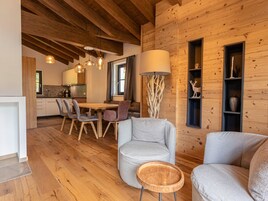 Um interior acolhedor com soalho de madeira, uma área de refeições com cadeiras, uma lâmpada e um sofá.