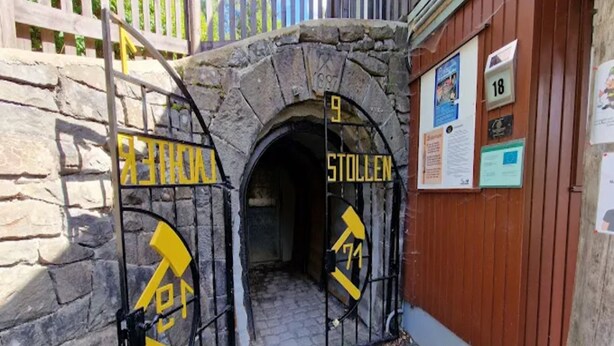 Um arco de pedra com uma placa indicando "STOLLE" e uma seta amarela apontando para a direita.