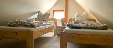 Um quarto de sótão pequeno e acolhedor, com duas camas beliches de madeira, uma mesinha e uma janela que oferece luz natural.
