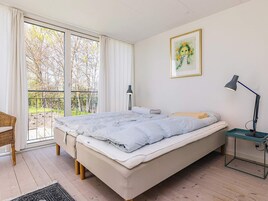 Quarto com uma cama grande, uma escrivaninha, uma cadeira, uma janela com cortinas e um quadro na parede.