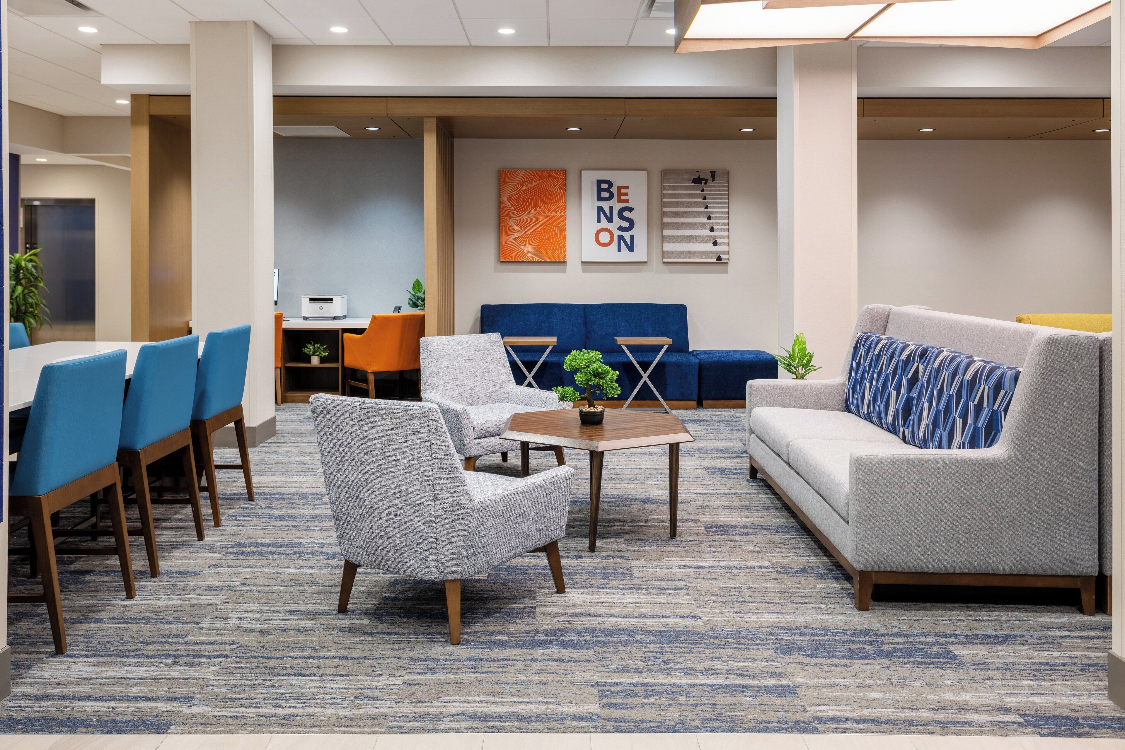Um lobby moderno com esquema de cores azul e cinza, apresentando uma mesa de recepção, área de estar com sofá e cadeiras, e uma mesa de centro com uma planta.