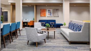 Um lobby moderno com esquema de cores azul e cinza, apresentando uma mesa de recepção, área de estar com sofá e cadeiras, e uma mesa de centro com uma planta.