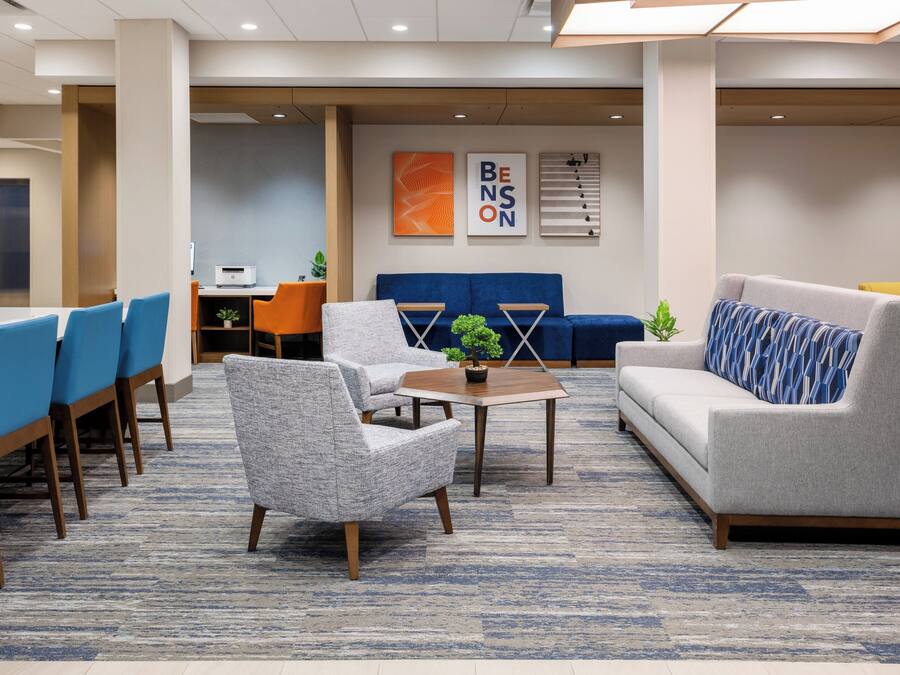 Um lobby moderno com esquema de cores azul e cinza, apresentando uma mesa de recepção, área de estar com sofá e cadeiras, e uma mesa de centro com uma planta.