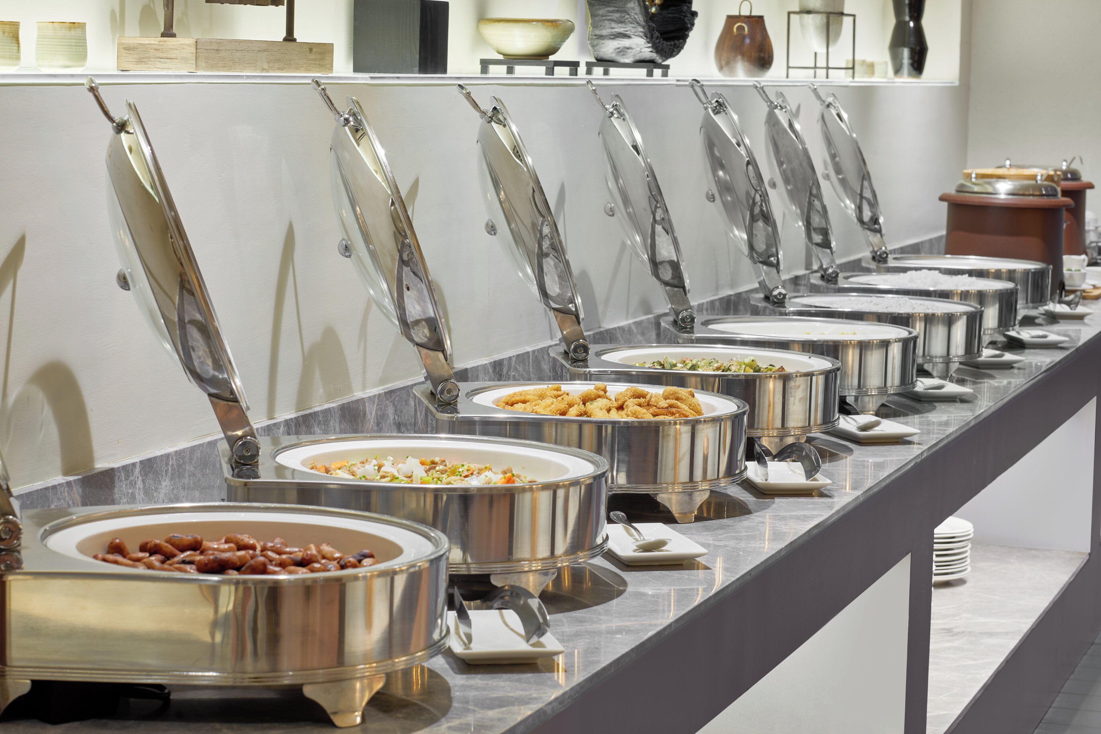 Disposição de buffet com várias estações de comida, cada uma com uma concha e um recipiente.