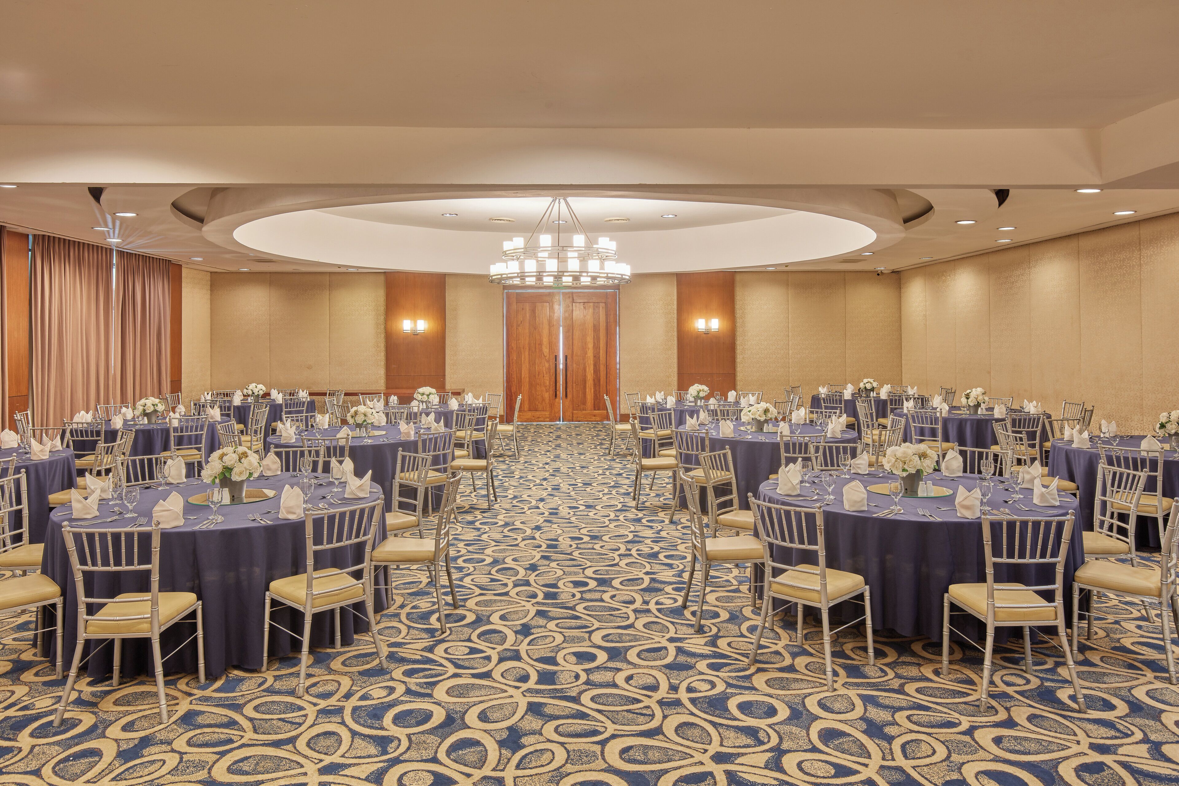 Uma sala de banquetes com mesas redondas, cadeiras e um tapete estampado.