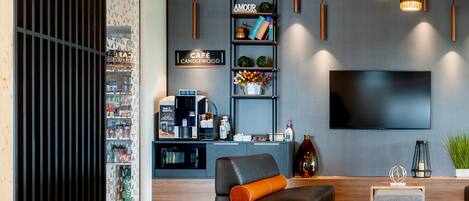 Uma sala de estar moderna com televisão de tela plana, máquina de café e estante de livros.