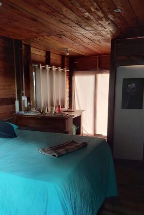 Quarto de cabana de madeira com cama, escrivaninha e janela com cortinas.