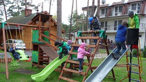 Um parquinho com uma estrutura de escalada de madeira, um escorrega verde e um escorrega vermelho.