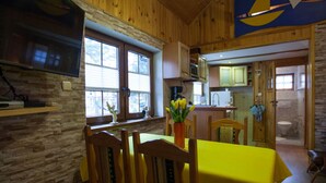 Interior em madeira com área de refeições, mesa e cadeiras amarelas, cozinha com armários de madeira e banheiro visível.