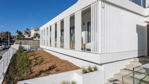 Um edifício moderno com fachada branca, grandes janelas e área ajardinada com plantas.