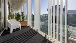 Uma varanda com cadeira de plástico branca, plantas em vasos e vista para um muro branco e edifícios.