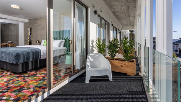 Quarto de hotel moderno com uma cama grande, uma porta de vidro que dá para uma varanda e vista da cidade.