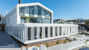 Um edifício moderno de dois andares, com grandes janelas de vidro, uma varanda com área de estar externa e uma cerca branca de piquete.