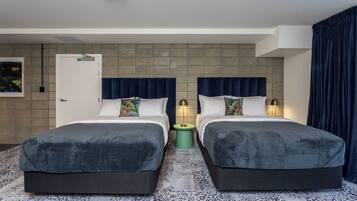 Quarto de hotel com duas camas, uma mesa de apoio verde e um tapete estampado.