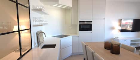 Uma cozinha moderna com armários brancos, forno embutido e área de refeições com mesa e cadeiras de madeira.