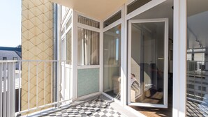Uma varanda com piso xadrez, guarda-corpo branco e porta de vidro que dá para o interior.