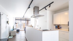 Cozinha moderna com ilha central, armários brancos e coifa de aço inoxidável.
