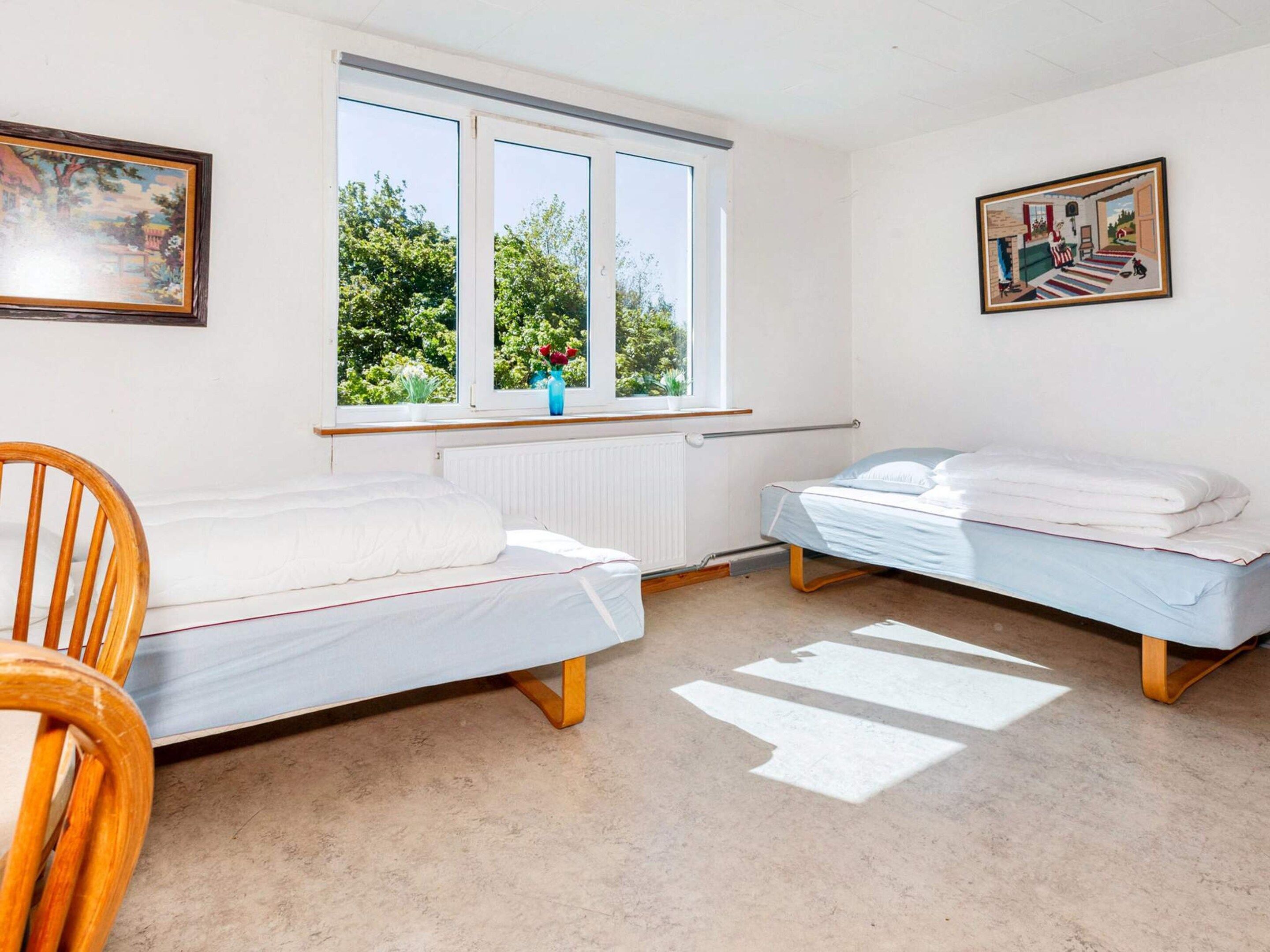 Quarto com duas camas, janela com vista para o verde e uma cadeira.