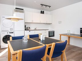 Cozinha moderna com armários brancos, forno embutido e máquina de café. Há uma mesa de jantar com cadeiras e um lustre.