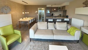 Sala moderna com sofá, mesa de jantar e cozinha visível por uma porta aberta.